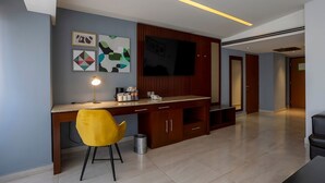 Uma sala de estar moderna com uma escrivaninha de madeira, uma poltrona amarela, uma TV fixada na parede e obras de arte.
