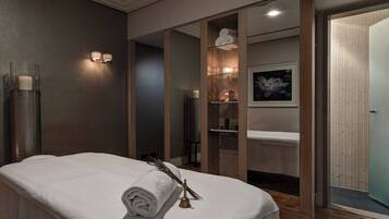 Um espaço de spa com uma mesa de massagem, um armário de madeira com toalhas e uma prateleira com velas.