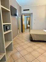 Quarto de hotel com cama, televisão fixada na parede, guarda-roupa e chão em azulejo.