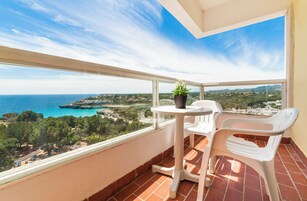 Uma varanda com mesa e cadeiras, um vaso de planta e vista para o mar e paisagem.