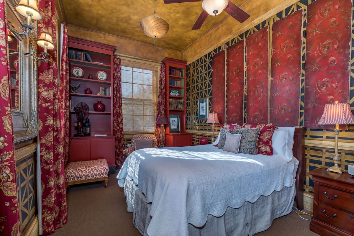 Quarto com uma cama grande, um guarda-roupa de madeira, um pequeno banco e uma estante de livros.