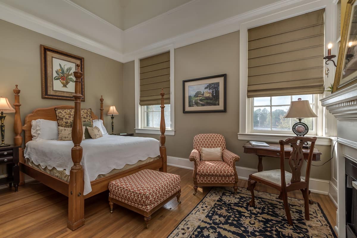 Quarto com cama de dossel, escrivaninha de madeira, cadeira e lareira.