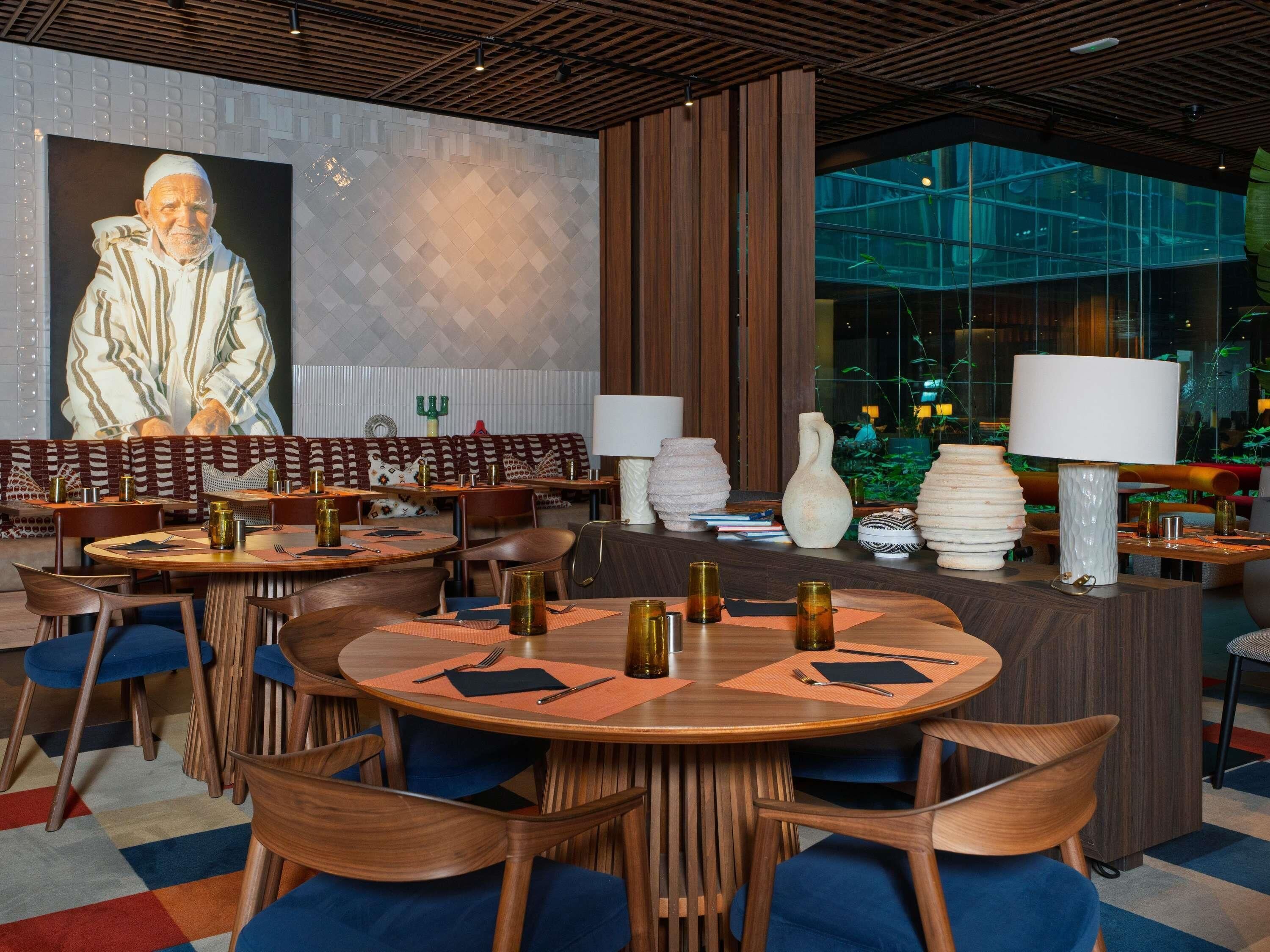 Um restaurante moderno com mesas redondas, cadeiras azuis acolchoadas e um grande mural na parede.