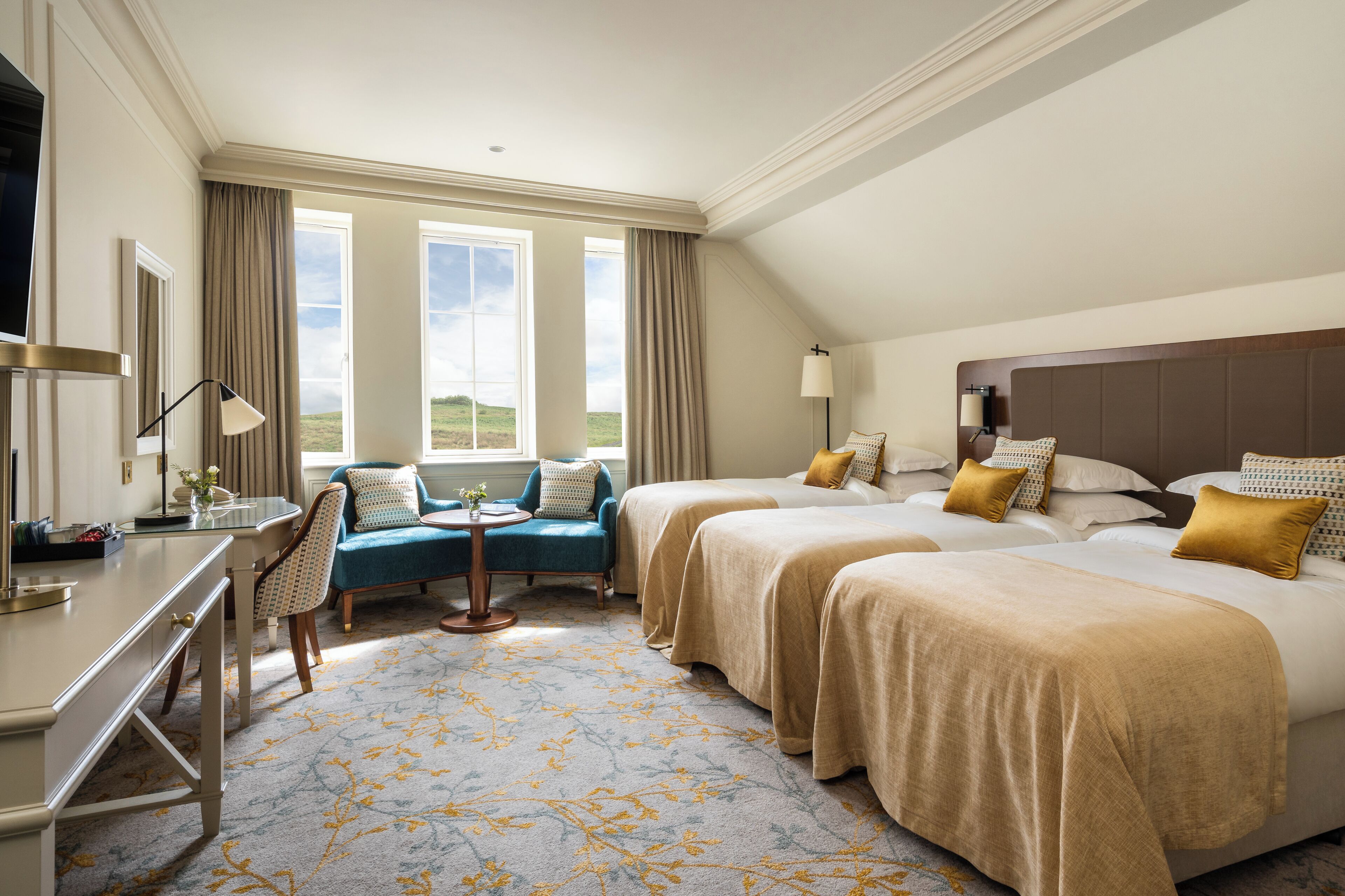 Quarto de hotel com duas camas, uma mesa, uma cadeira e vista para o exterior.