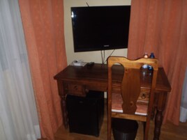 Uma escrivaninha de madeira com uma televisão de tela plana, uma cadeira e um cesto de lixo.