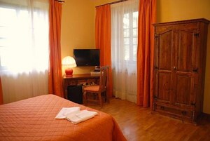 Quarto de hotel com uma cama, uma escrivaninha com luminária, televisão e guarda-roupa.