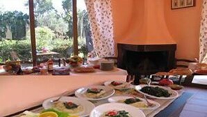 Uma sala de jantar com vários pratos de comida, uma lareira e vista para o verde lá fora.