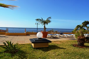 Terraço com palmeira, cadeiras de descanso e vista para o mar.