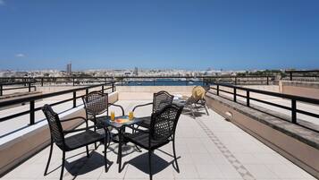 Terraço com mesa e cadeiras, com vista para um areal e o horizonte da cidade.