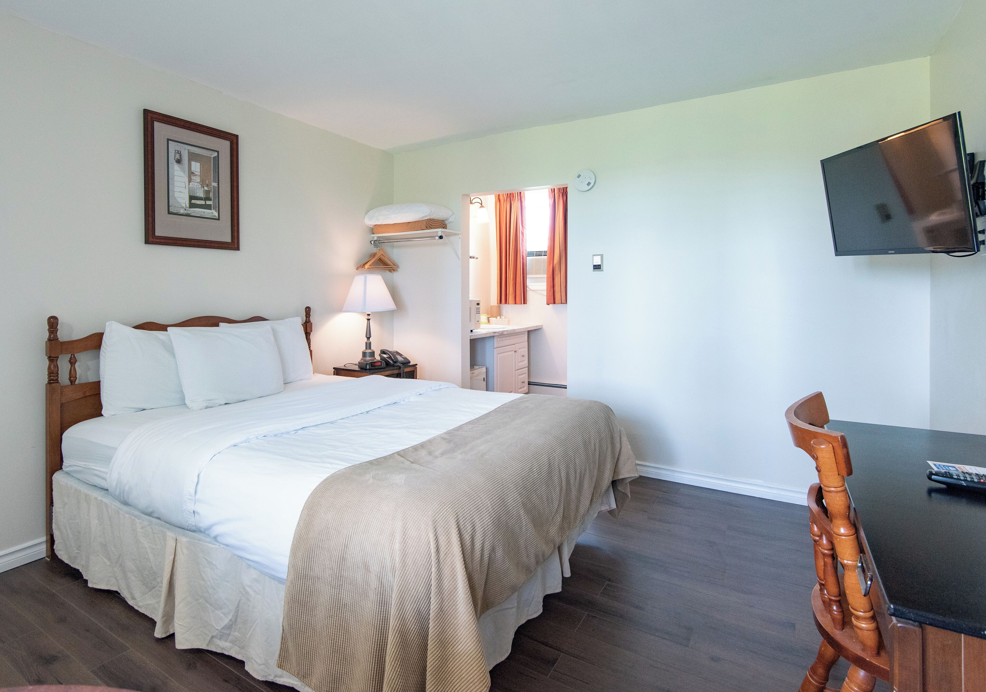 Quarto de hotel com cama, mesa de cabeceira, abajur e televisão presa na parede.