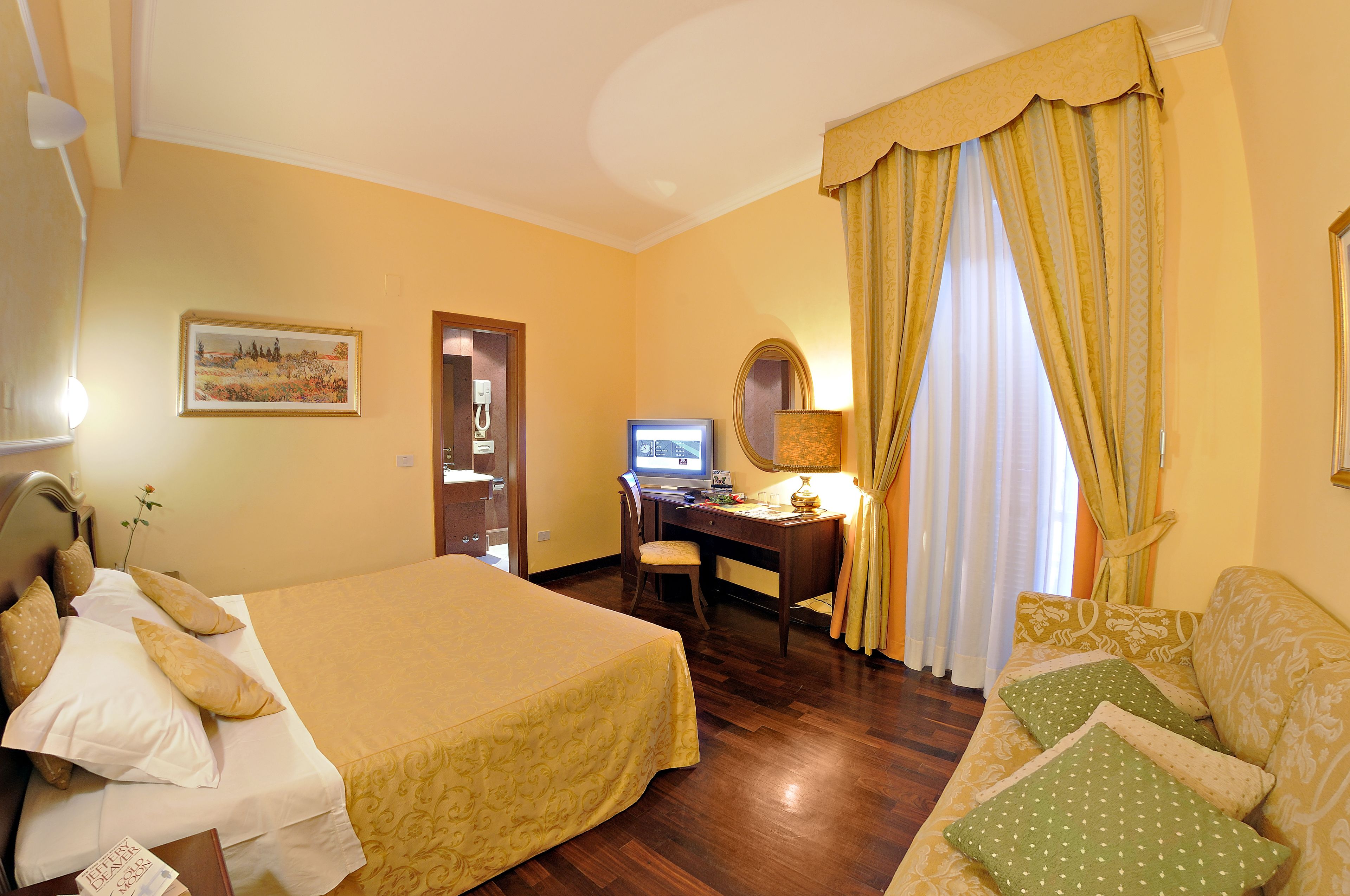 Quarto de hotel com cama, escrivaninha, computador, cadeira e sofá.