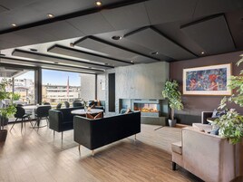 Um lounge moderno com lareira, assentos confortáveis e grandes janelas com vista para a cidade.