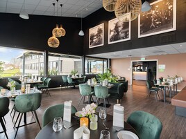 Um restaurante com cadeiras de veludo verde, mesas de madeira escura e iluminação pendente.