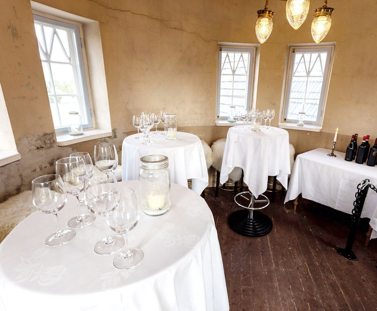 Restaurante com mesas redondas preparadas para refeições, cada uma com copos de vinho e velas.