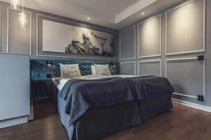 Quarto moderno com uma cama grande, parede azul de destaque e uma grande pintura abstrata sobre a cama.