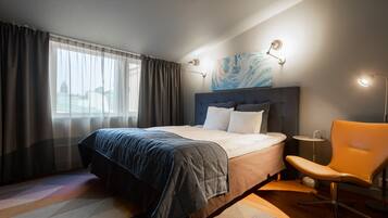 Quarto de hotel com uma cama, uma cadeira, uma mesinha de cabeceira e um quadro na parede.