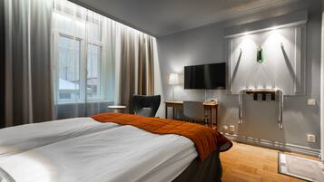 Quarto de hotel com uma cama grande, uma mesa, uma cadeira, uma TV e um porta-toalhas fixado na parede.