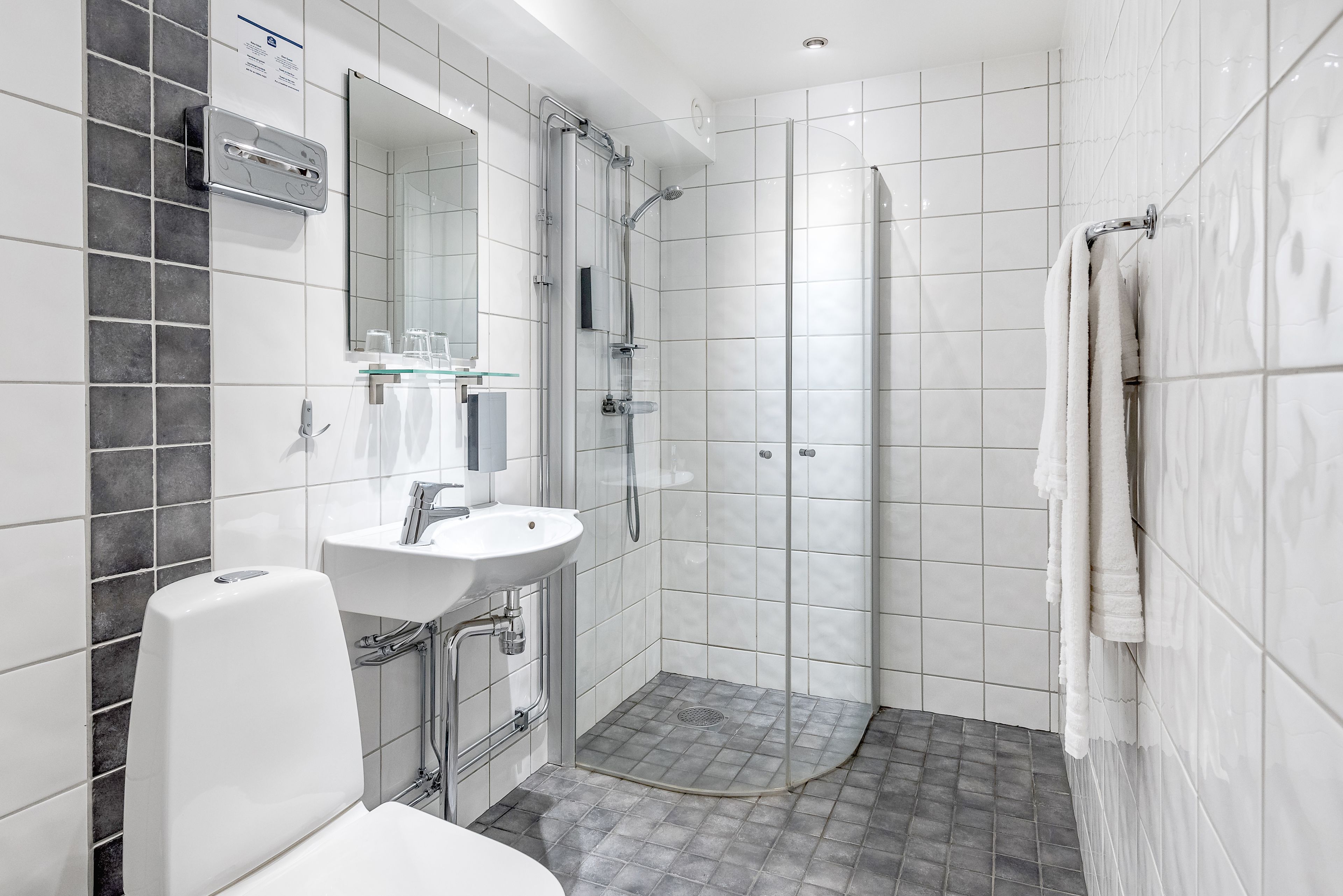 Casa de banho moderna com lavatório branco, espelho e chuveiro.