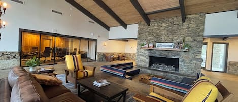 Uma sala de estar ampla com lareira de pedra, sofás de couro e teto de madeira.