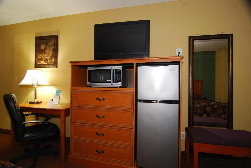 Quarto de hotel com escrivaninha de madeira, uma cadeira, televisão, micro-ondas e frigorífico.