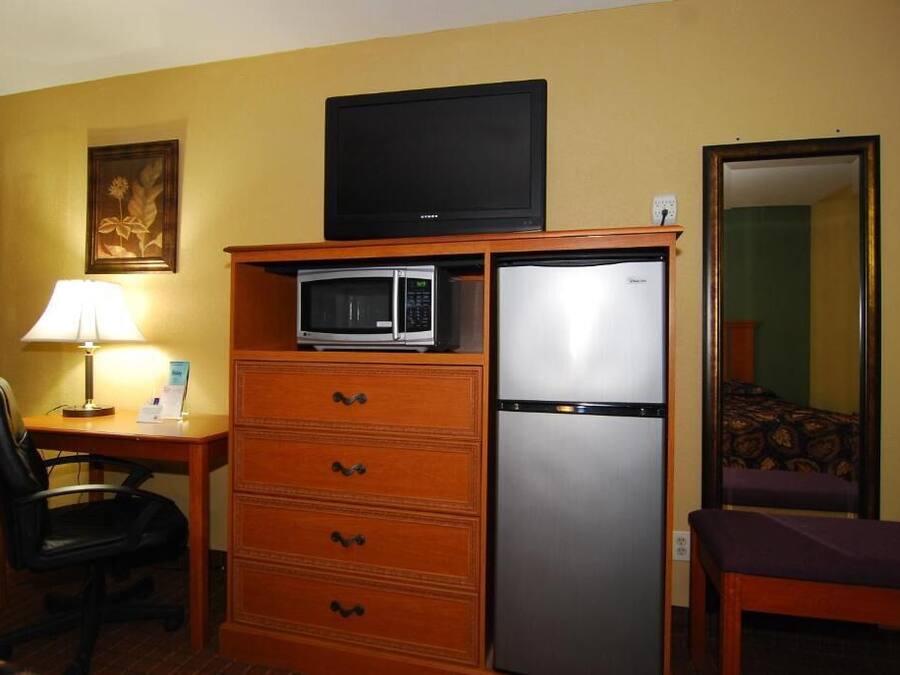 Quarto de hotel com escrivaninha de madeira, uma cadeira, televisão, micro-ondas e frigorífico.