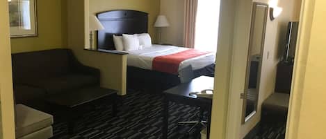 Quarto de hotel com cama, escrivaninha, cadeira, sofá e uma mesinha.