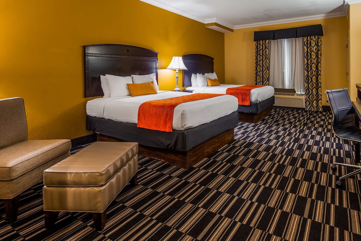 Quarto de hotel com duas camas, uma escrivaninha, uma cadeira e um pequeno sofá.