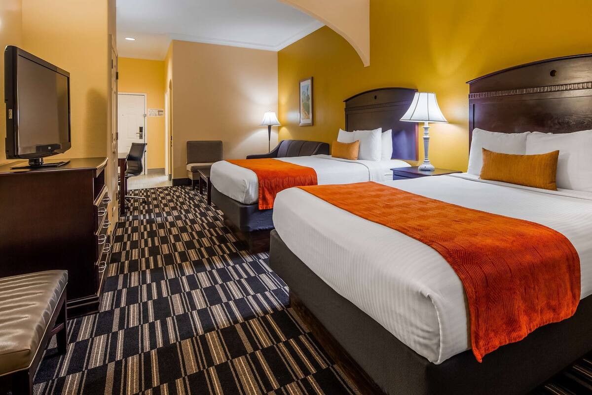Quarto de hotel com duas camas, televisão, escrivaninha e carpete estampado.