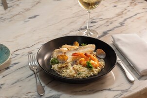 Prato de risoto de frutos do mar com amêijoas e camarões, um garfo, uma taça de vinho e um guardanapo sobre uma mesa de mármore.