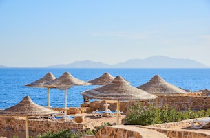 Um resort à beira-mar com paredes de pedra, guarda-sóis de palha e espreguiçadeiras.