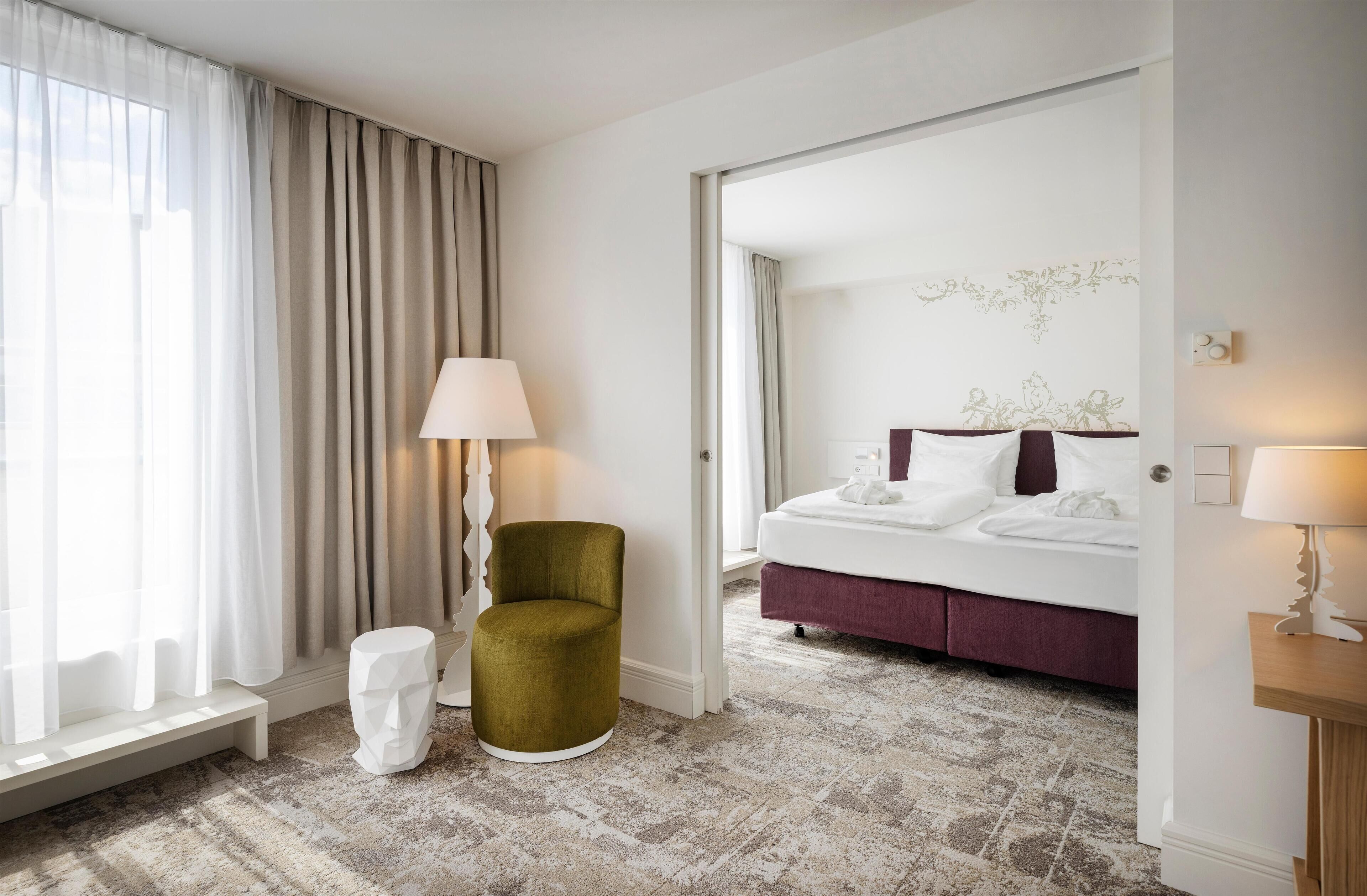 Quarto de hotel com cama, cadeira, abajur e um banco.