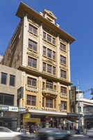 Um edifício de vários andares com estilo arquitetônico clássico, com grandes janelas e uma varanda no segundo andar.