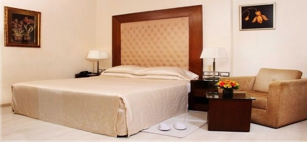 Quarto de hotel bem arrumado, com uma cama grande, um sofá, uma mesa de cabeceira com luminárias e uma pequena mesa com um vaso de flores.