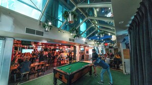Espaço de lazer coberto com mesa de bilhar, áreas de estar e bar.