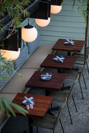 Um restaurante com mesas e cadeiras de madeira, um banco e luminárias pendentes.