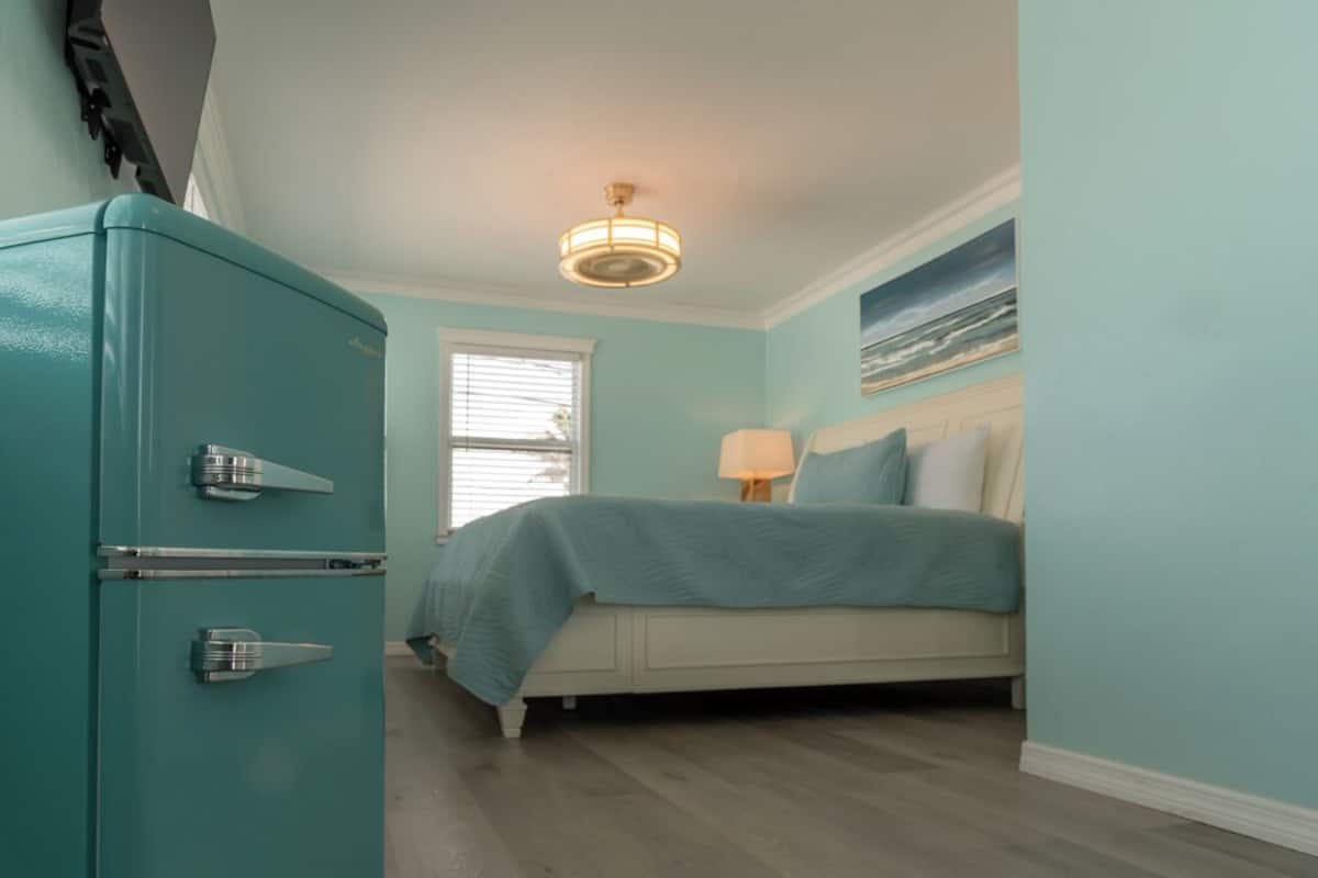 Quarto com cama, frigorífico azul-turquesa, janela e luminária no teto.