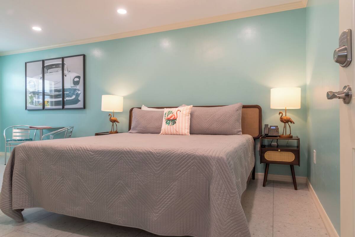 Quarto com cama, duas mesas de cabeceira com luminárias, uma cadeira e uma obra de arte na parede.