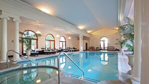 Piscina interior com chão em mosaico, rodeada por espreguiçadeiras e um solário.
