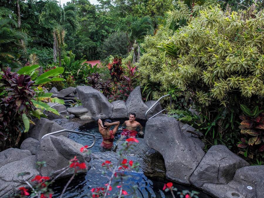 Uma nascente termal natural rodeada por pedras e vegetação exuberante.