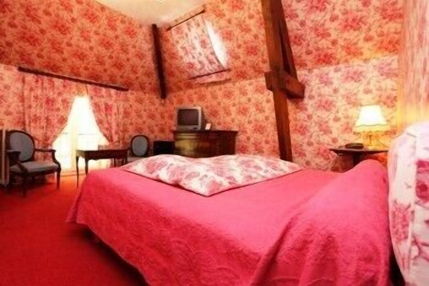 Quarto com cama, escrivaninha, cadeira, luminária e televisão.