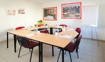 Uma sala de conferência com uma mesa grande, cadeiras vermelhas e um quadro branco.