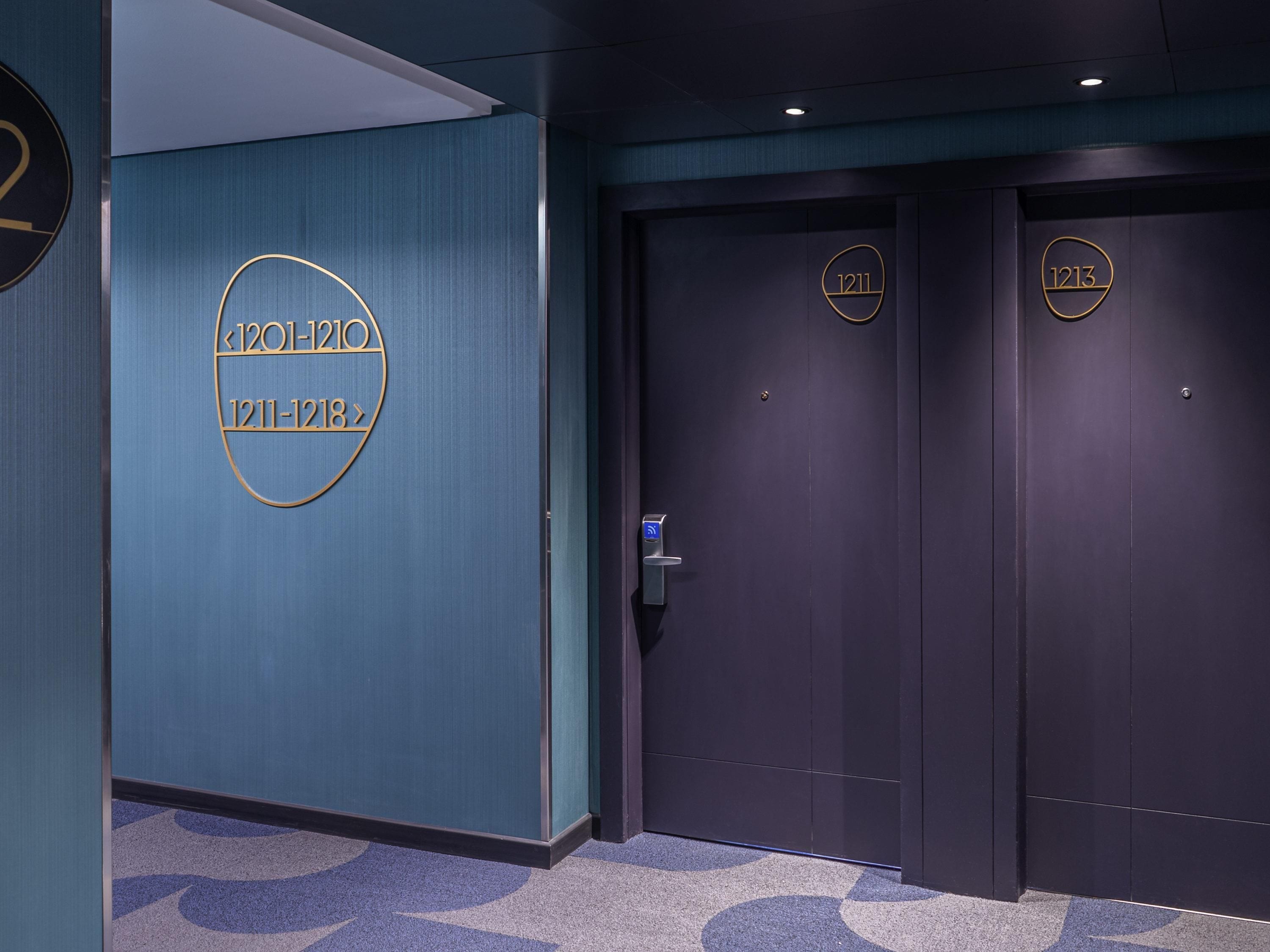 Corredor de hotel com duas portas identificadas com os números '1211' e '1213' e uma placa indicando os números de quarto '1201-1210' e '1211-1218'.