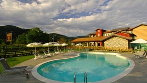 Uma piscina com espreguiçadeiras e guarda-sóis, rodeada por um edifício de pedra com fachada de pedra e cerca de madeira.