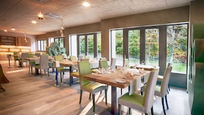 Um restaurante com mesas e cadeiras de madeira, janelas amplas e vista para as árvores.