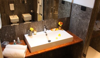 Casa de banho com uma pia branca, espelho, toalha e um vaso de flores.