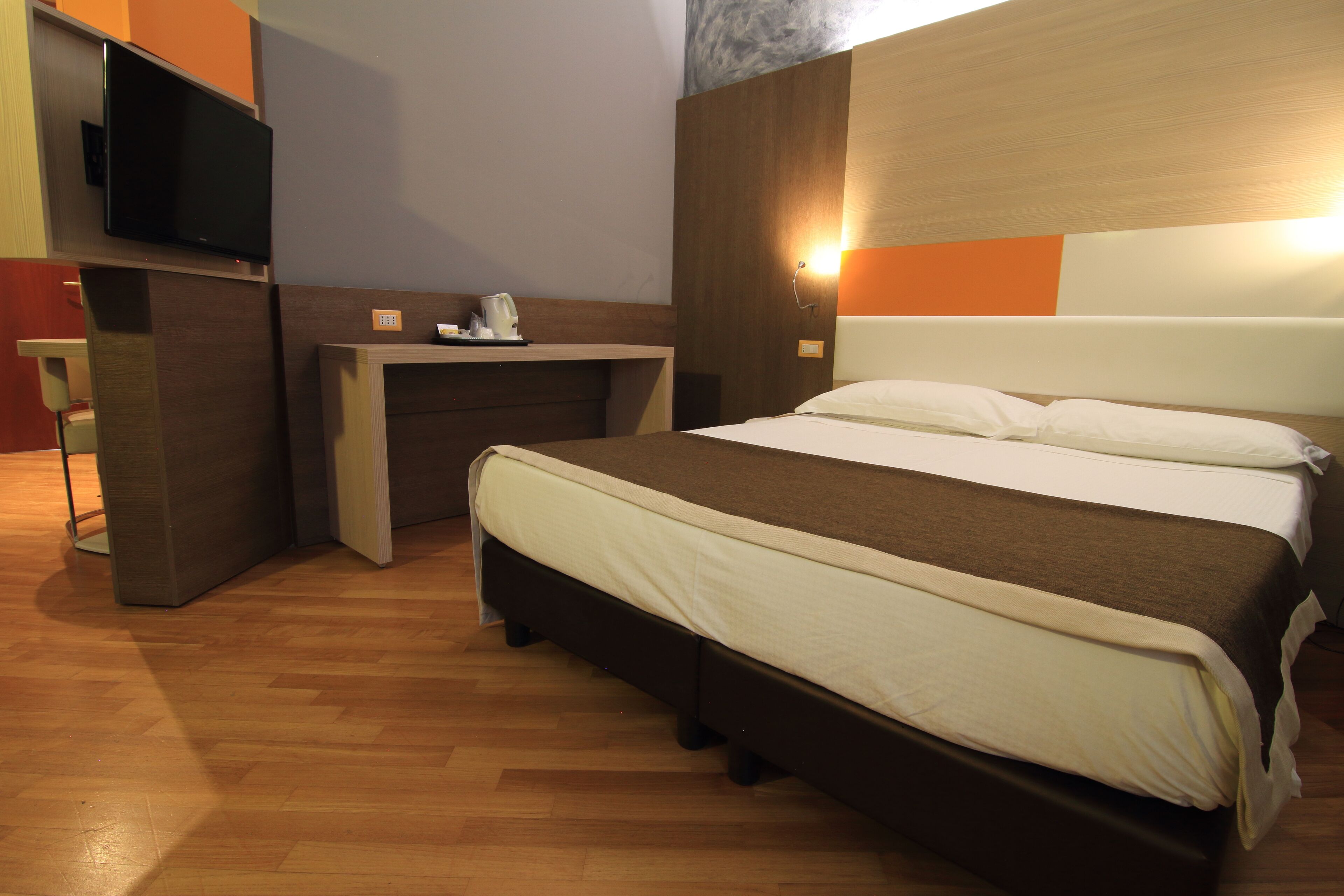 Quarto de hotel com cama, escrivaninha e televisão.