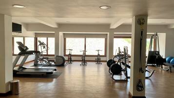 Uma academia ampla, equipada com máquinas de cardio, equipamentos de musculação e grandes janelas que proporcionam iluminação natural.