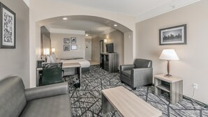Quarto de hotel com cama, duas poltronas, uma mesinha, escrivaninha com cadeira, televisão e luminária.