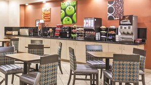Uma área de pequenos-almoços com lugares, uma máquina de café e um balcão com alimentos.