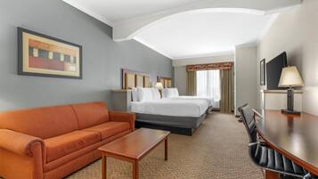 Quarto de hotel com cama, sofá, escrivaninha e televisão.